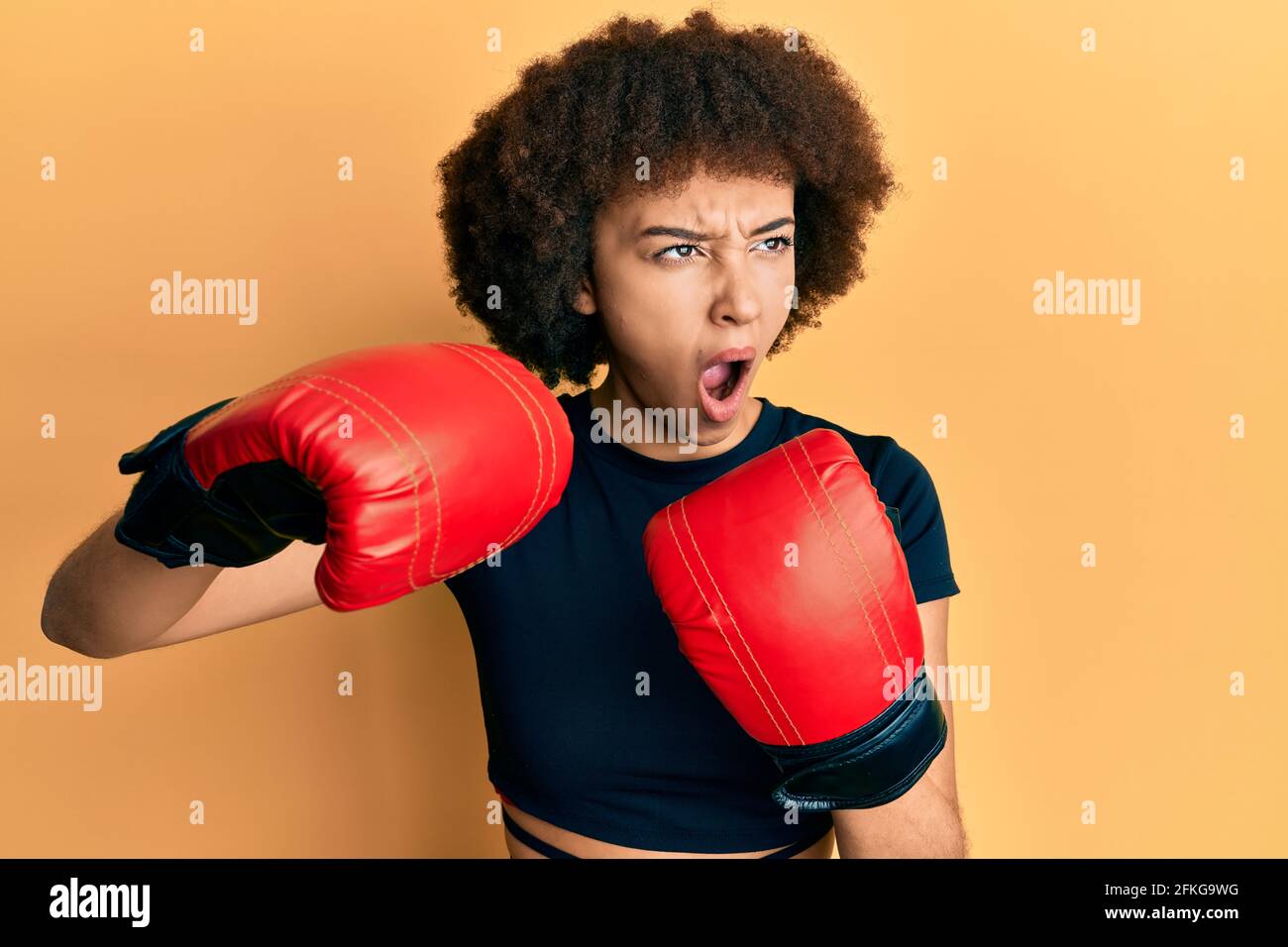 Young hispanic sporty girl using boxing gloves angry and mad screaming ...