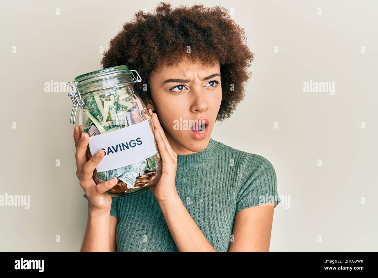 Young hispanic girl holding jar with savings angry and mad screaming ...