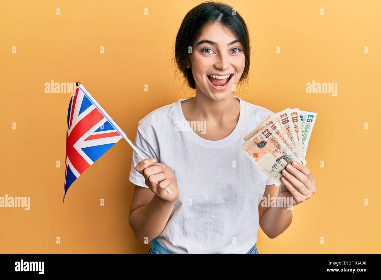 Young caucasian woman holding uk flag and pounds banknotes smiling and ...