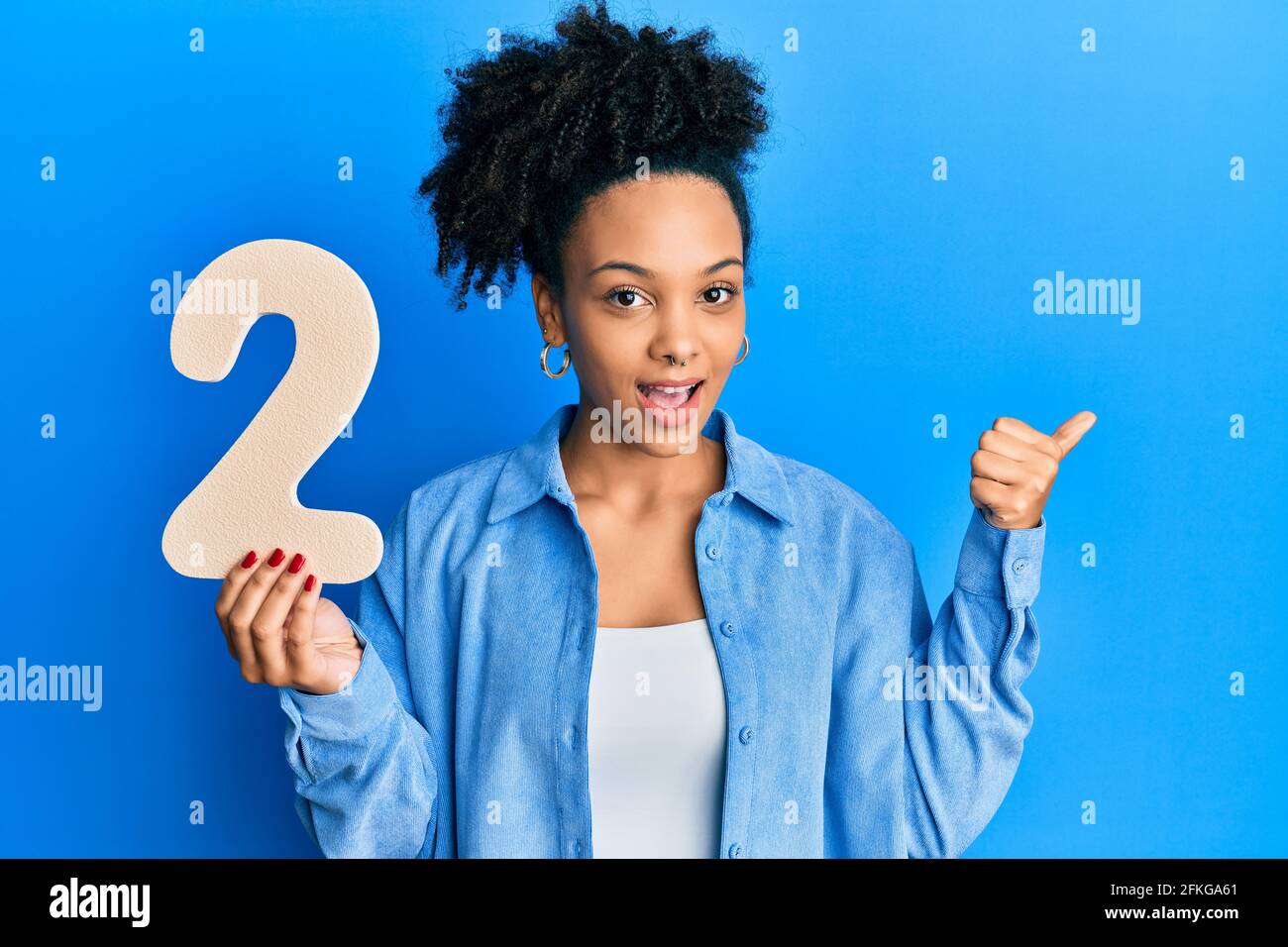 Young african american girl holding number two pointing thumb up to the ...