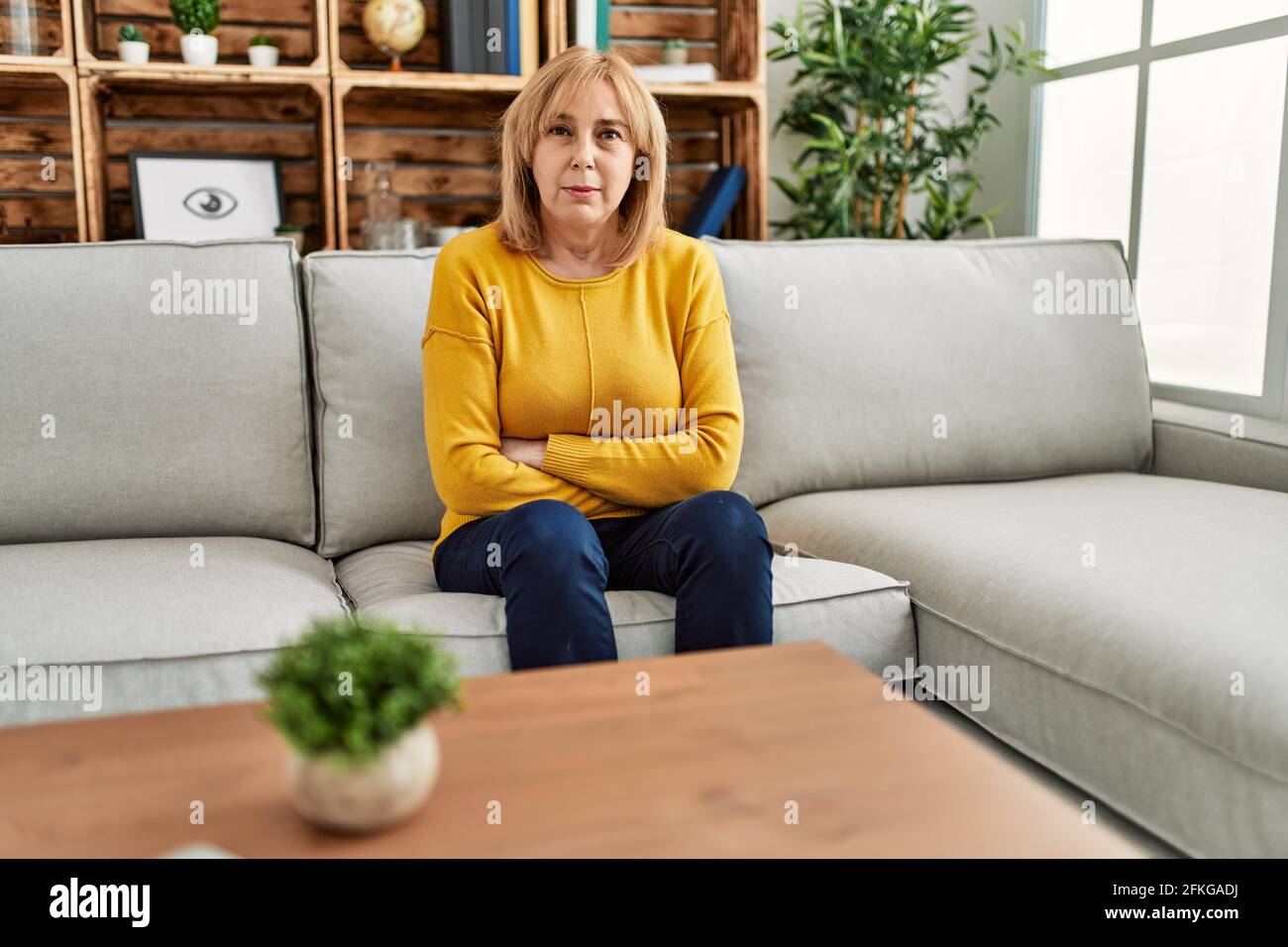 Middle age caucasian woman wearing casual clothes sitting on the sofa at home skeptic and ...
