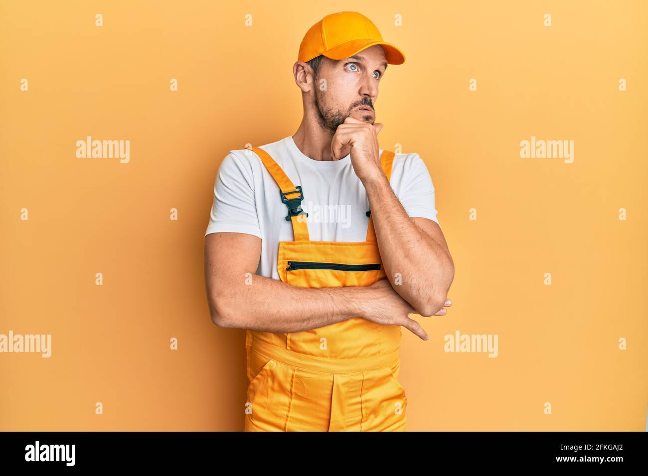 Young handsome man wearing handyman uniform over yellow background ...