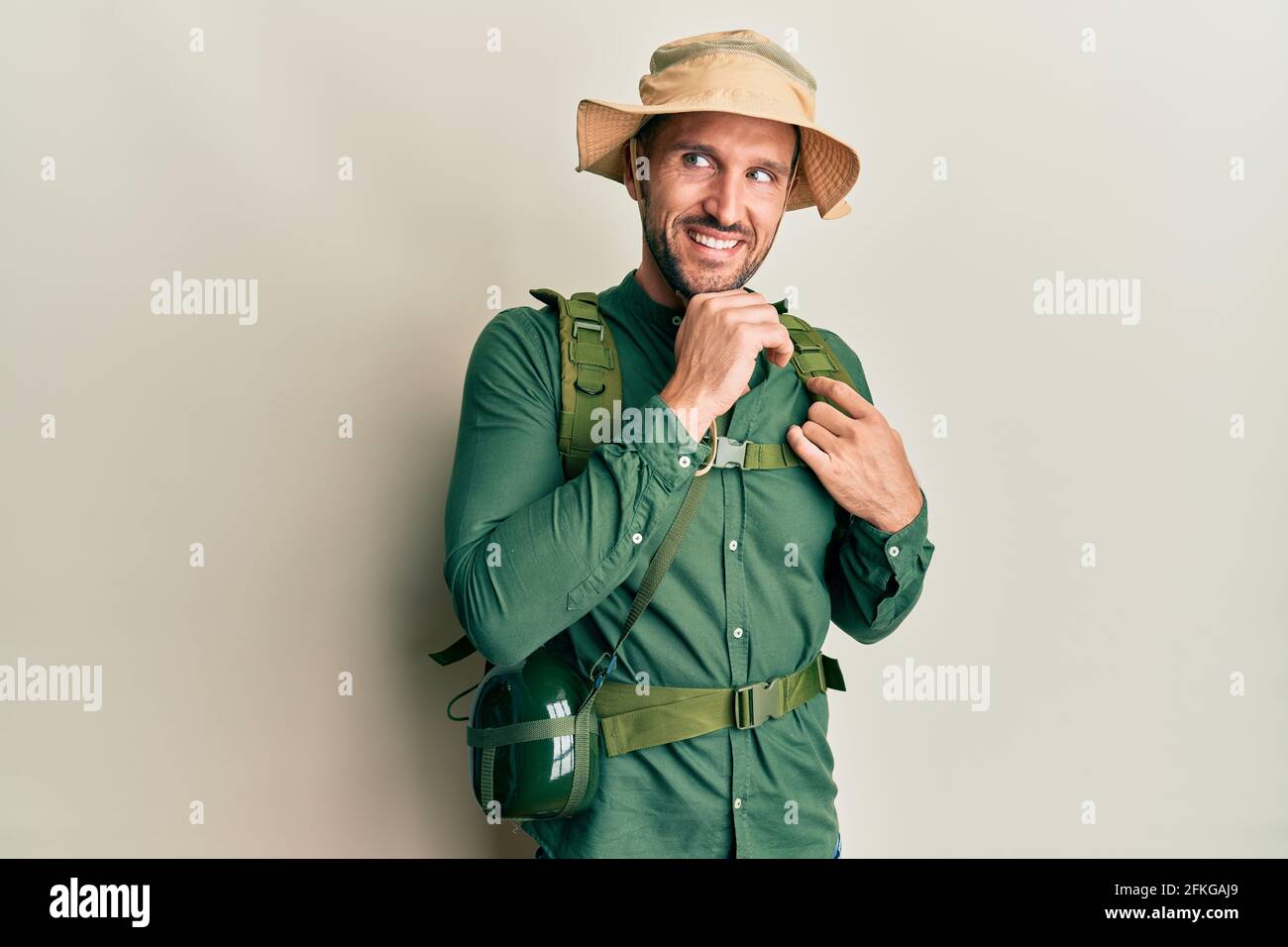 Handsome man with beard wearing explorer hat and backpack with hand on ...