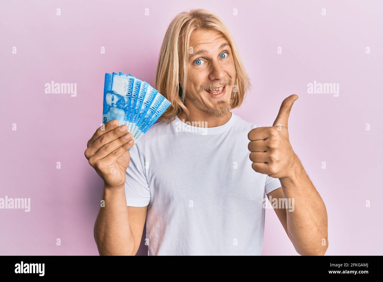 Caucasian young man with long hair holding 10000 chilean pesos smiling ...