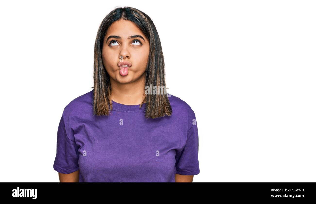 Young hispanic girl wearing casual purple t shirt making fish face with ...
