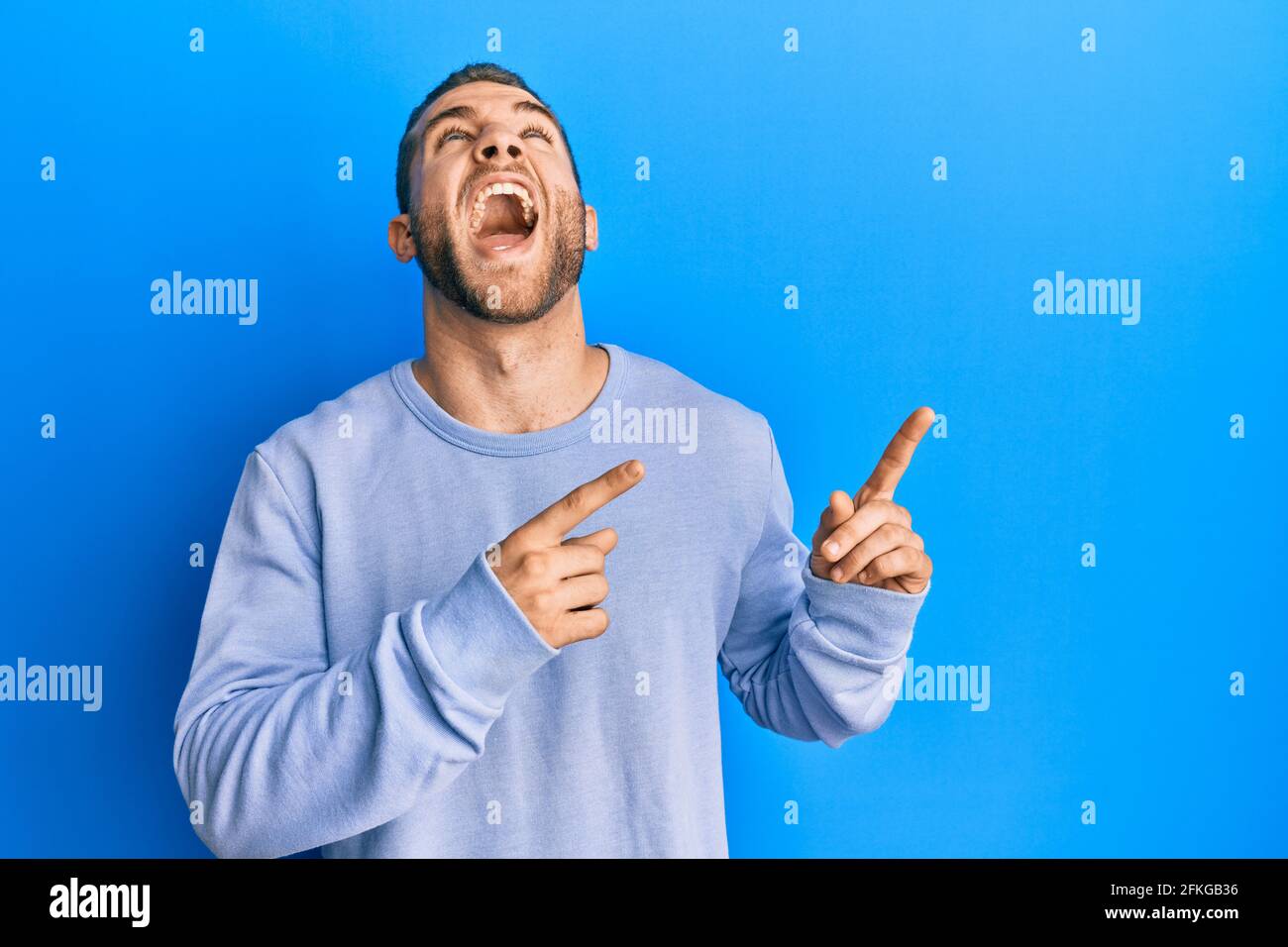 Young caucasian man pointing with fingers to the side angry and mad ...
