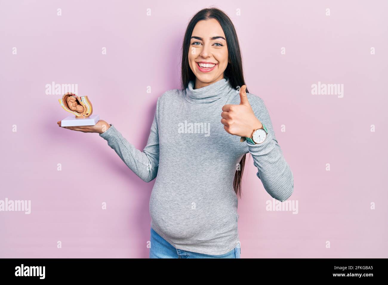 Beautiful woman with blue eyes expecting a baby, holding anatomic fetus ...
