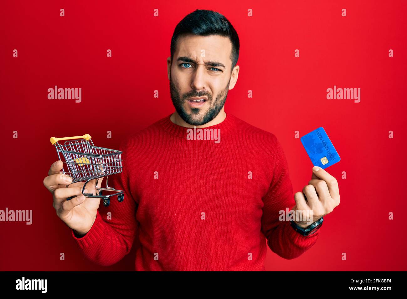 Young hispanic man holding small supermarket shopping cart and credit ...