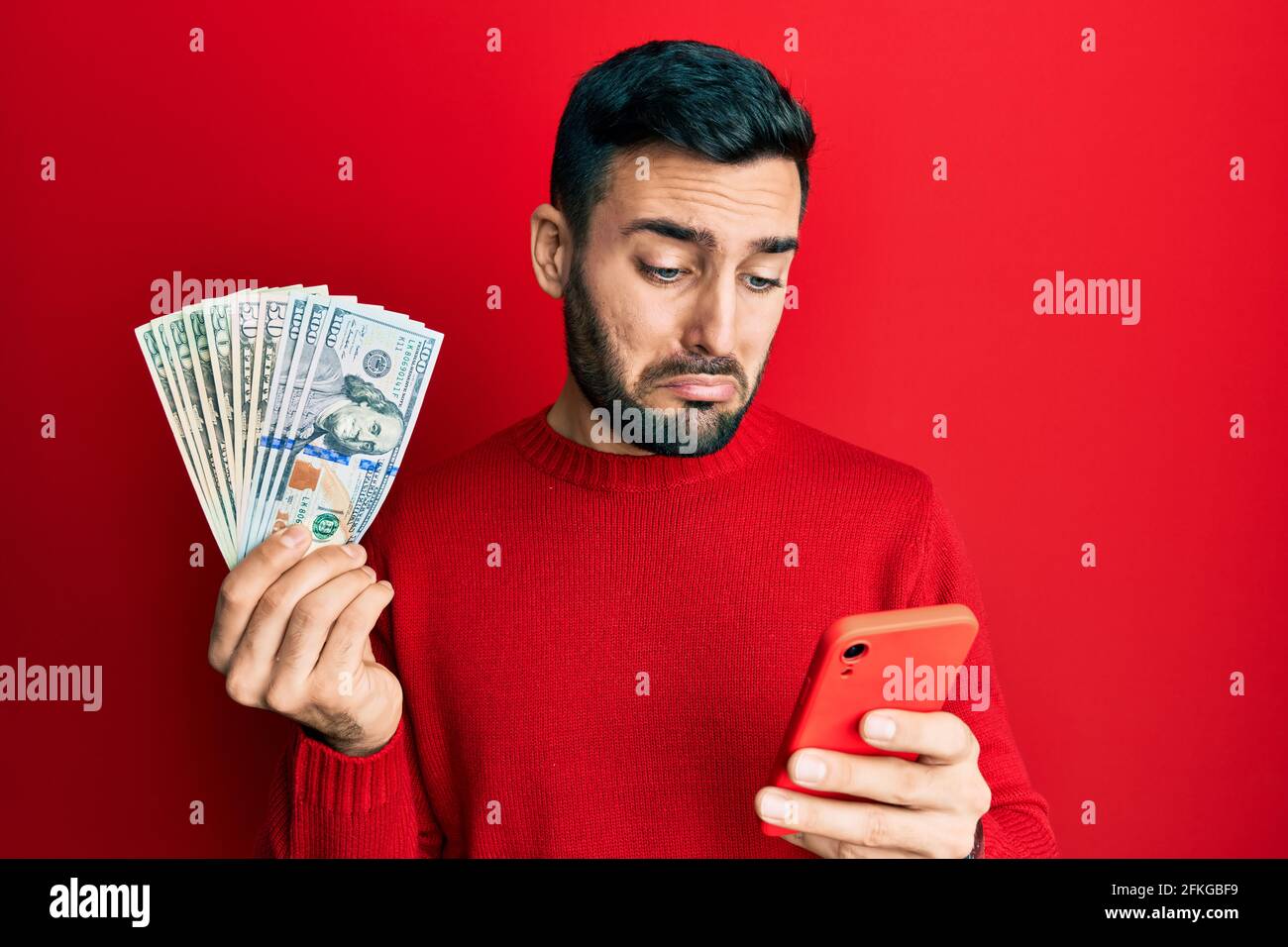Young hispanic man using smartphone holding usa dollars banknotes ...