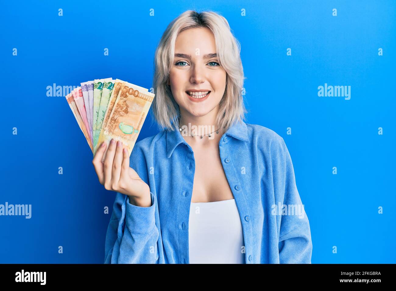 Young blonde girl holding philippine peso banknotes looking positive ...