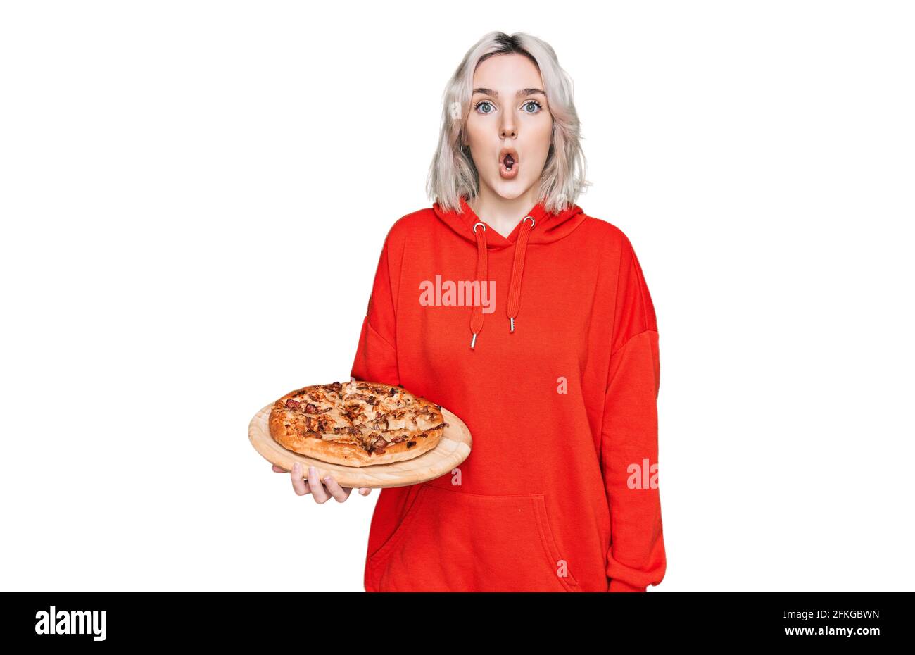 Young blonde girl holding italian pizza scared and amazed with open ...