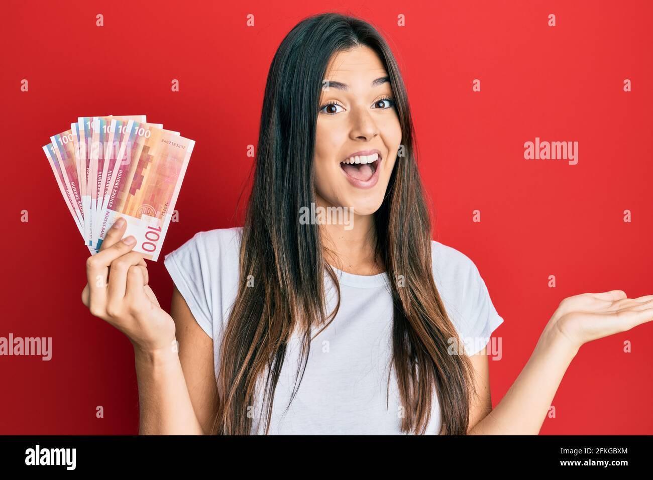 Young brunette woman holding 100 norwegian krone banknotes celebrating ...