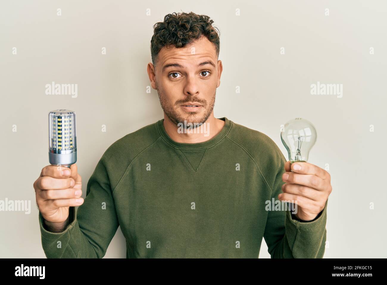 Young hispanic man holding lightbulb for inspiration and idea clueless ...