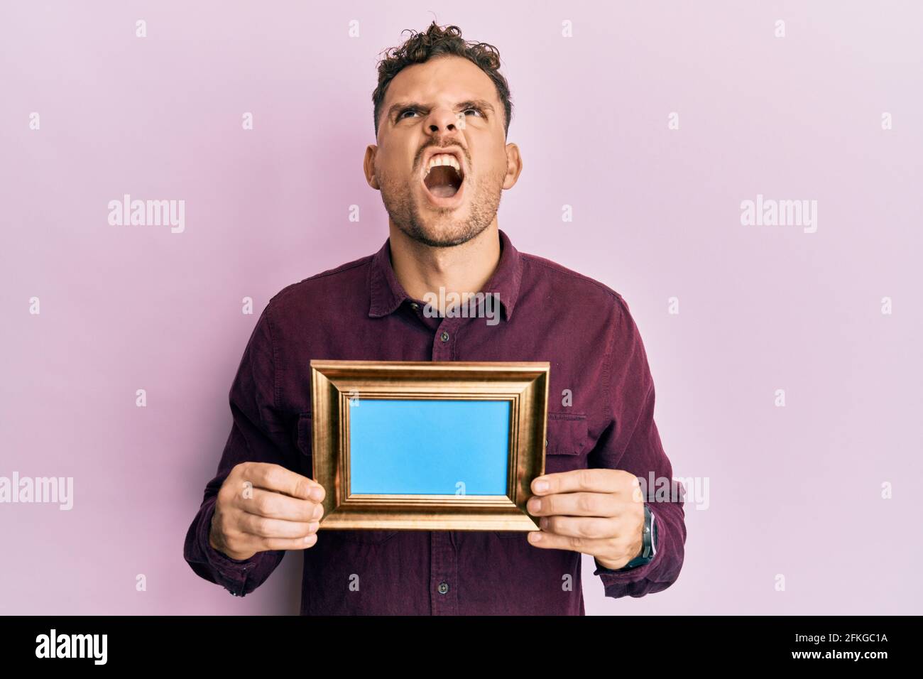 Young hispanic man holding empty frame angry and mad screaming ...