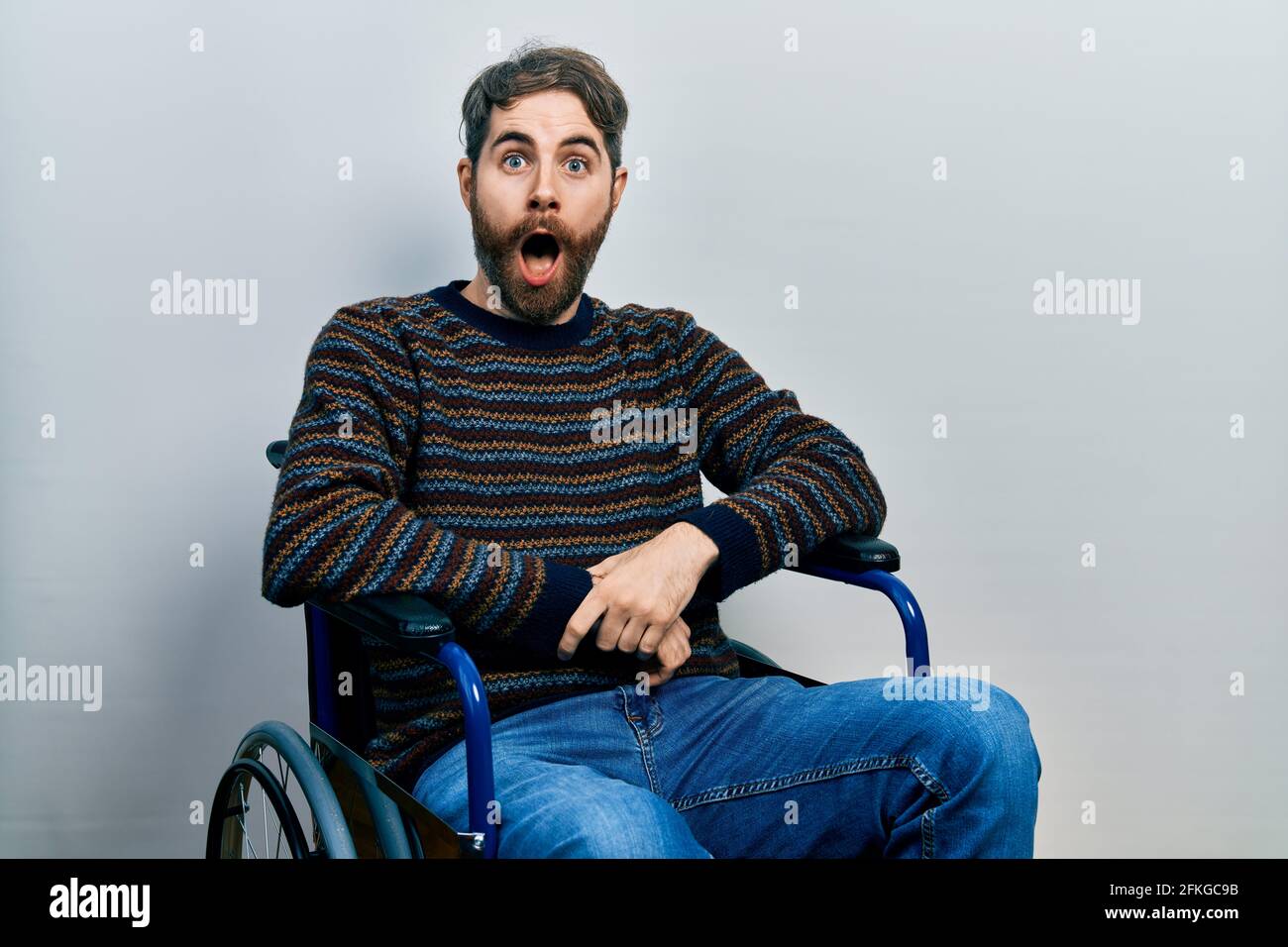 Caucasian man with beard sitting on wheelchair scared and amazed with ...