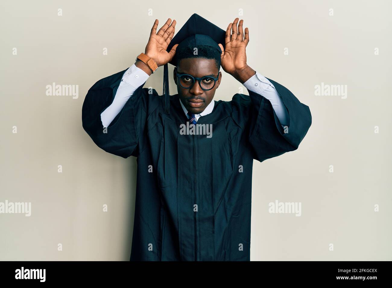 Handsome black man wearing graduation cap and ceremony robe doing bunny ...