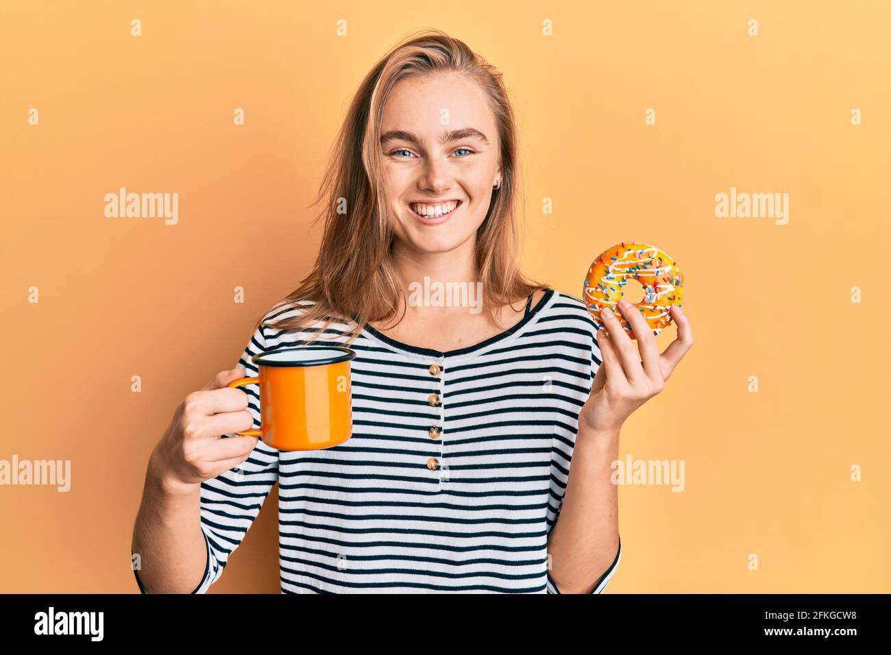 Beautiful blonde woman eating doughnut and drinking coffee smiling with ...