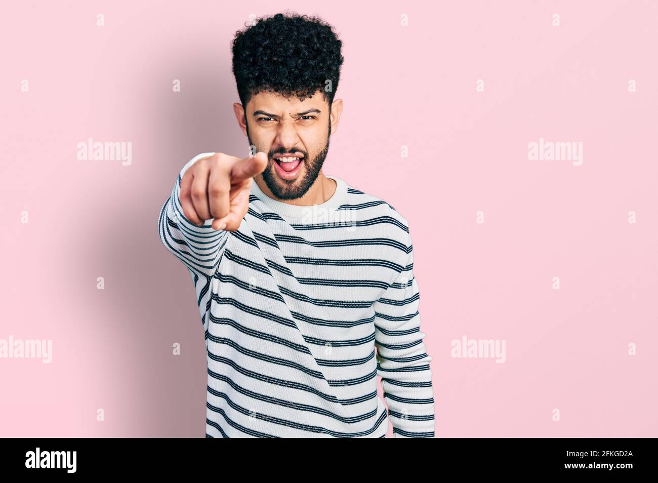 Young arab man with beard wearing casual striped sweater pointing ...
