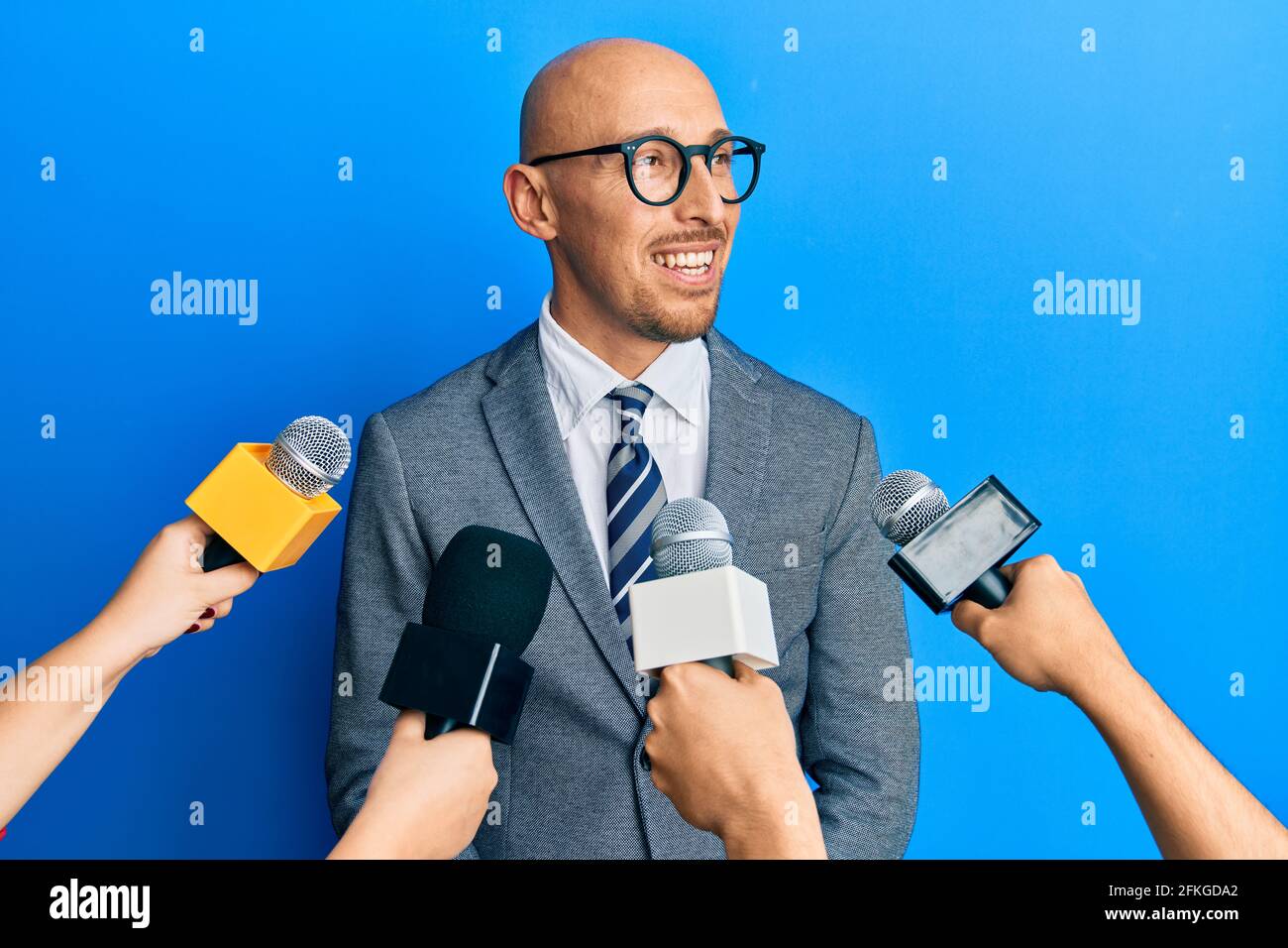 Bald man with beard being interviewed by reporters holding microphones ...