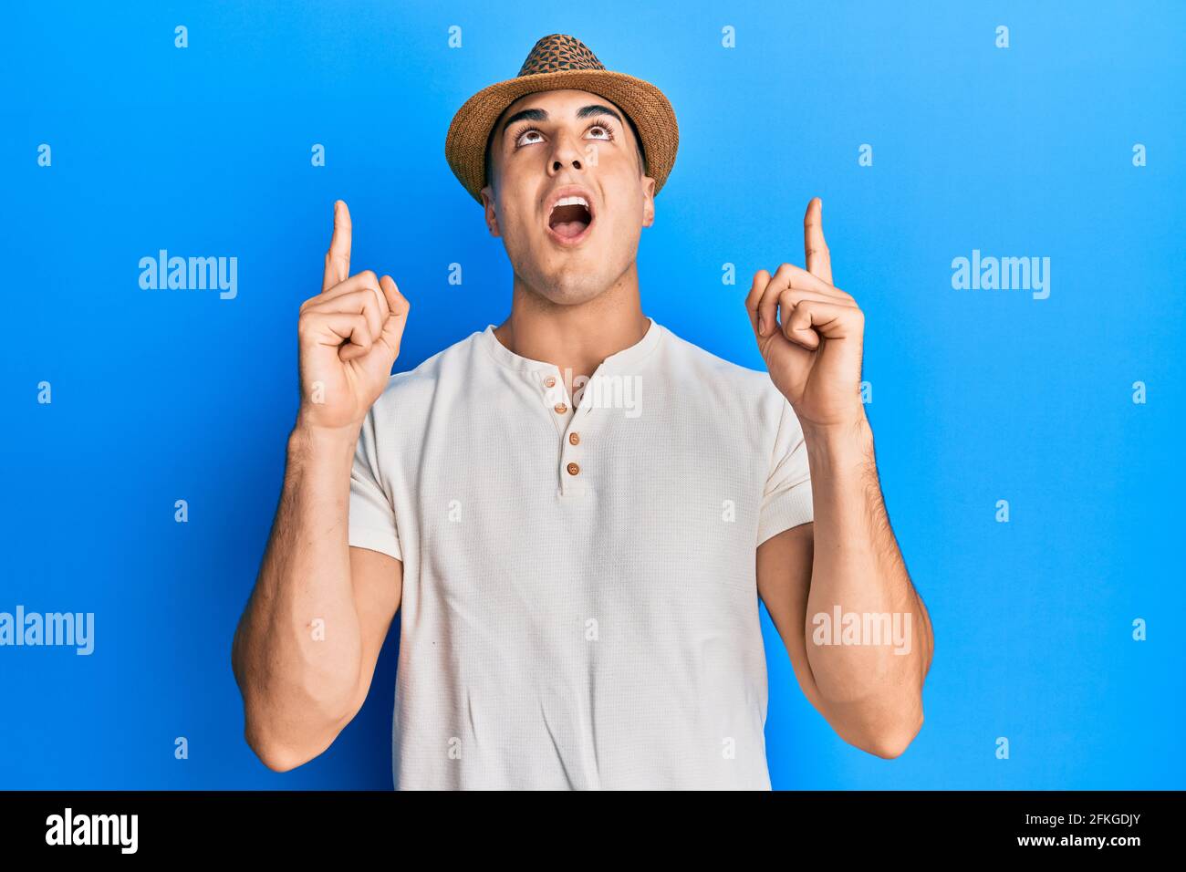 Hispanic young man wearing summer hat amazed and surprised looking up ...