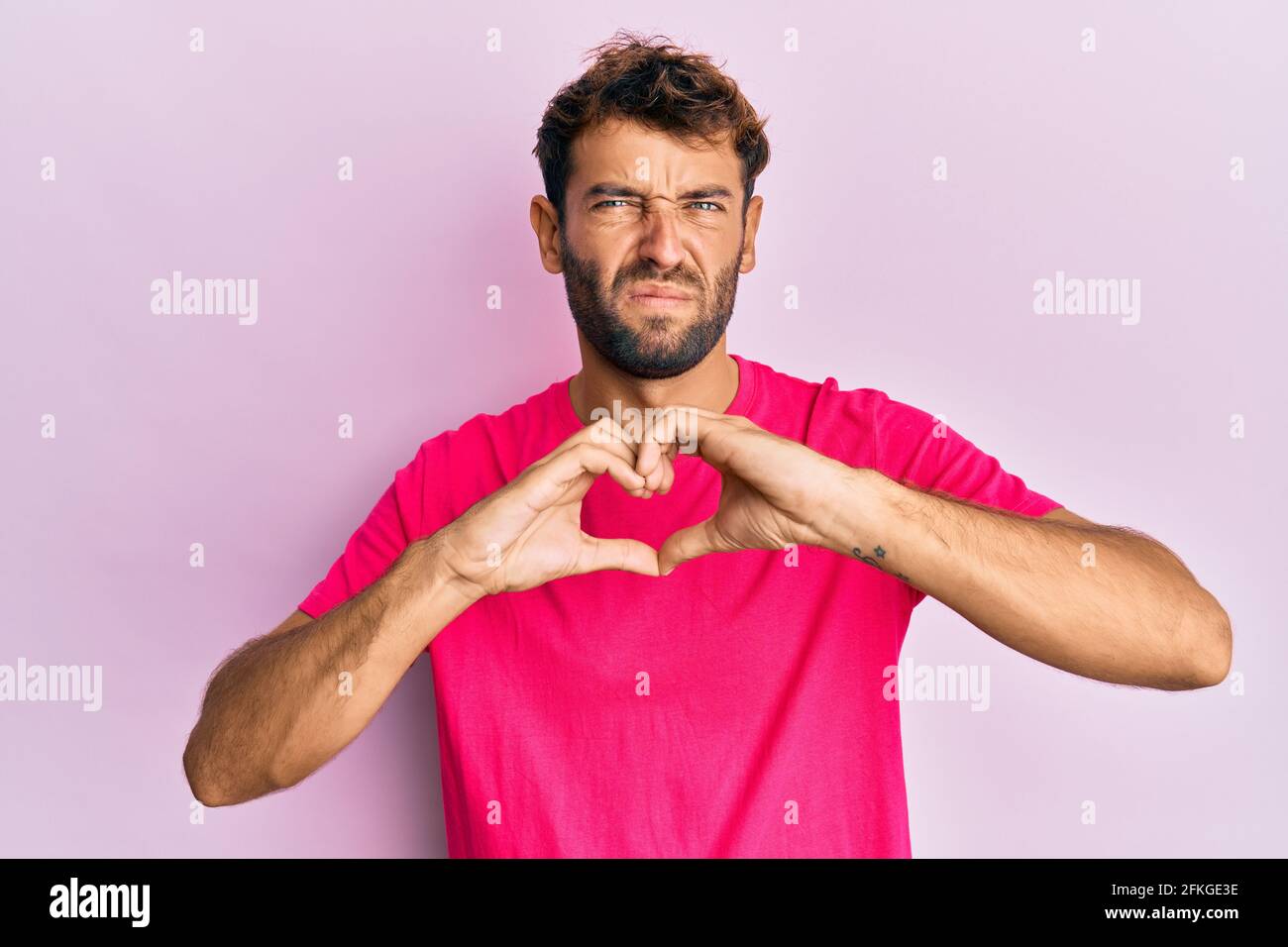 Handsome man with beard making heart symbol with hands shape skeptic ...