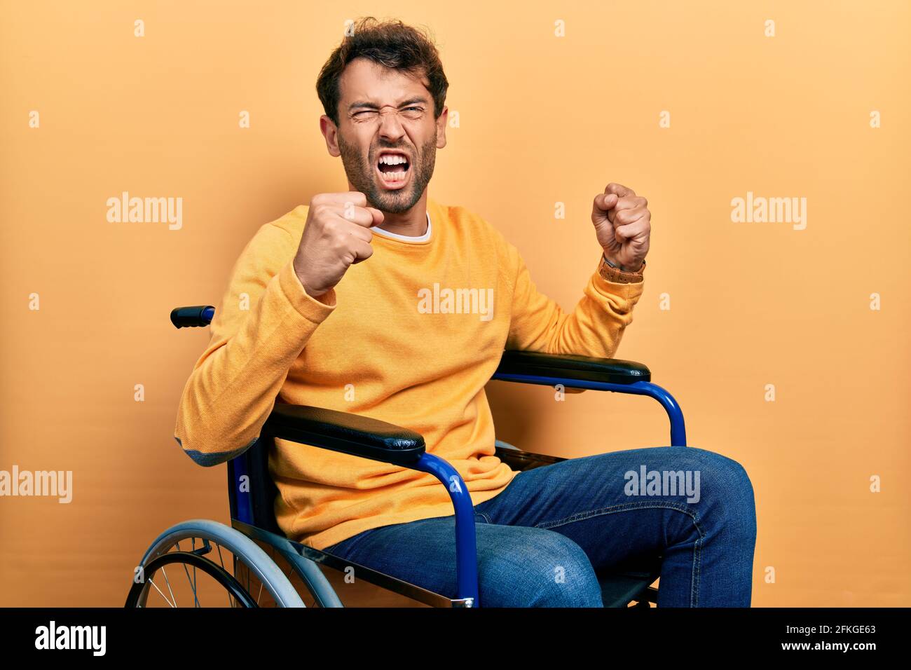 Handsome man with beard sitting on wheelchair angry and mad raising ...