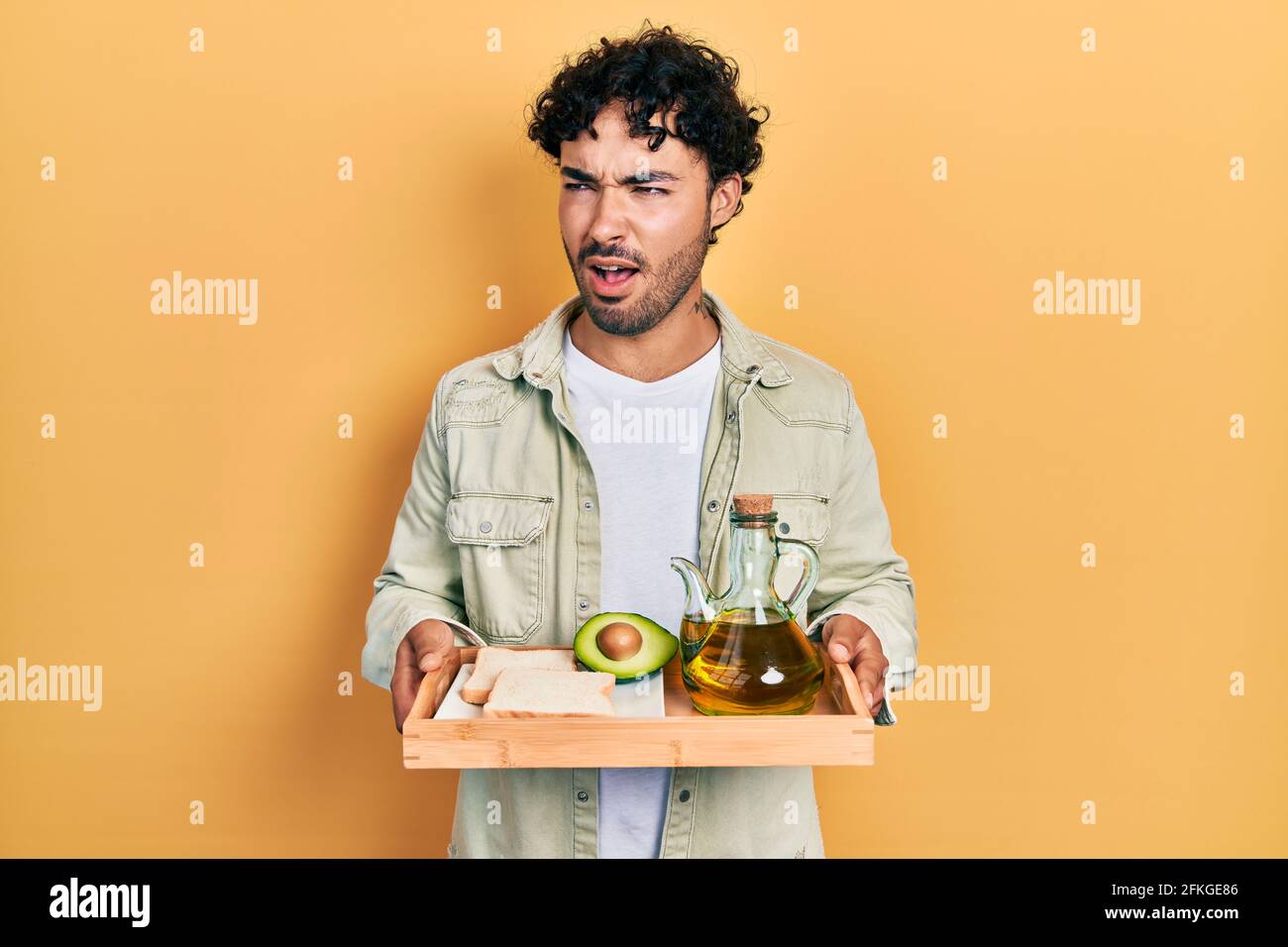 Young hispanic man holding tray with breakfast food angry and mad ...