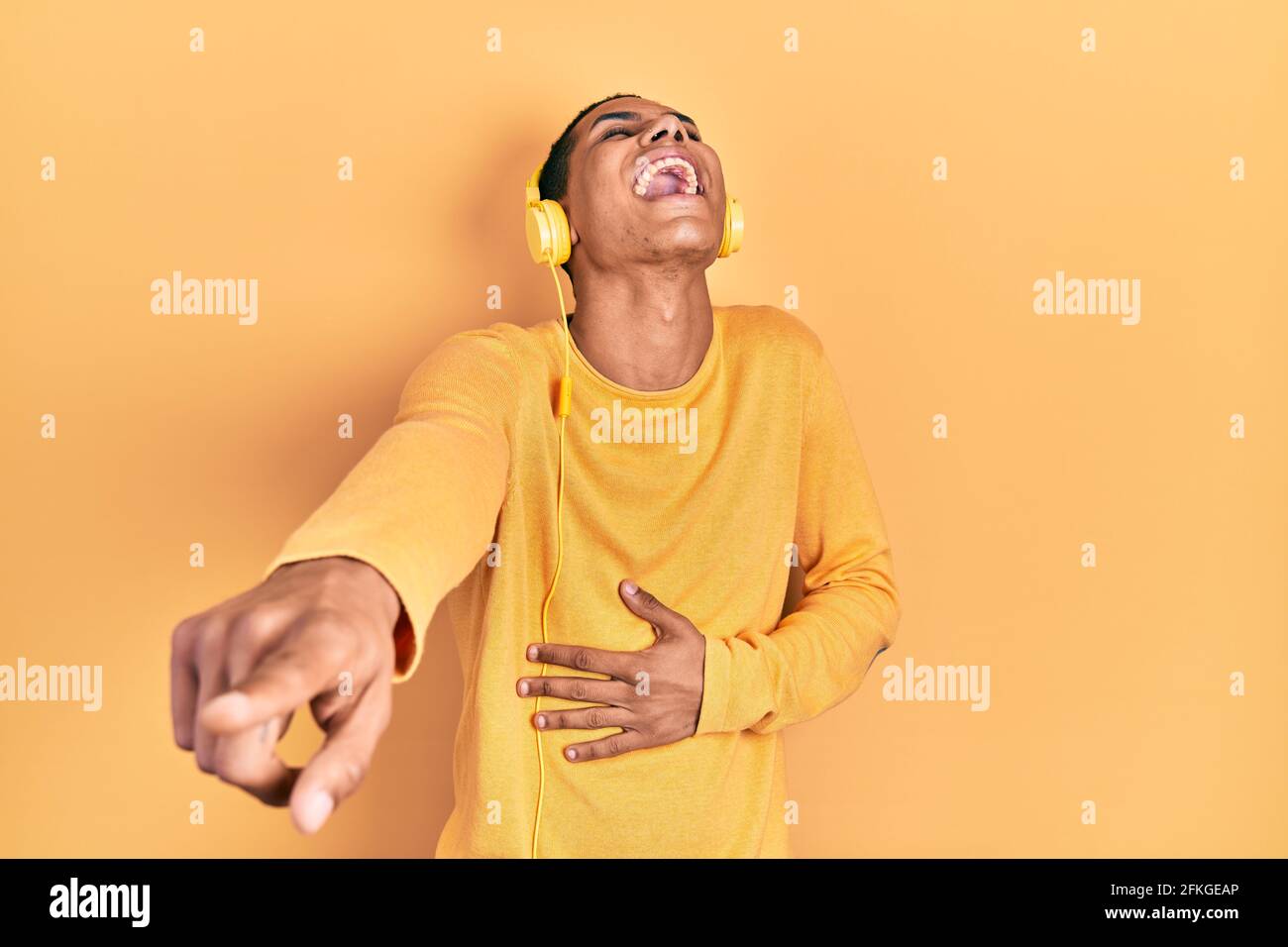 Young african american guy listening to music using headphones laughing ...