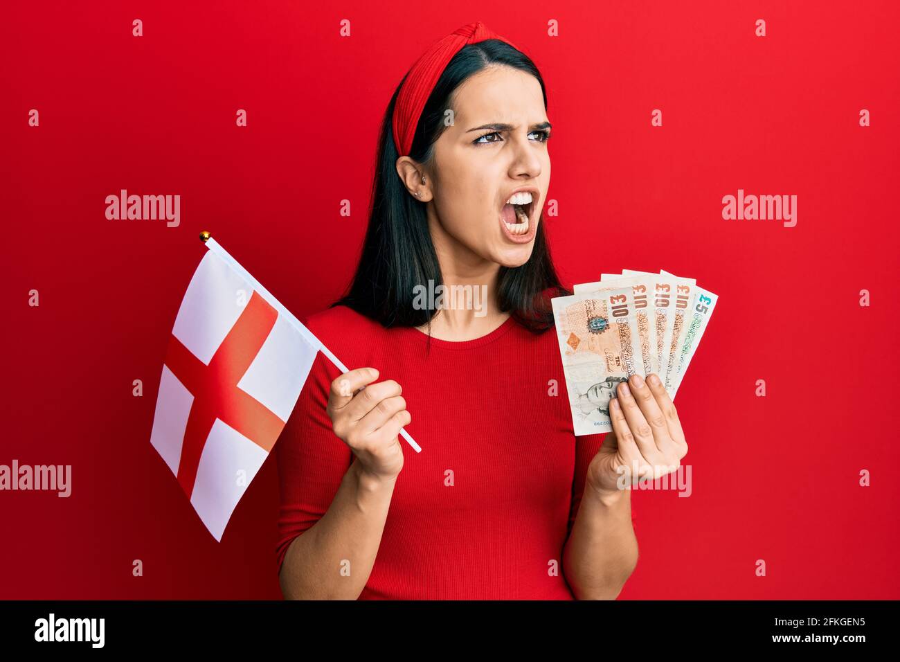 Young hispanic woman holding england flag and pounds banknotes angry ...