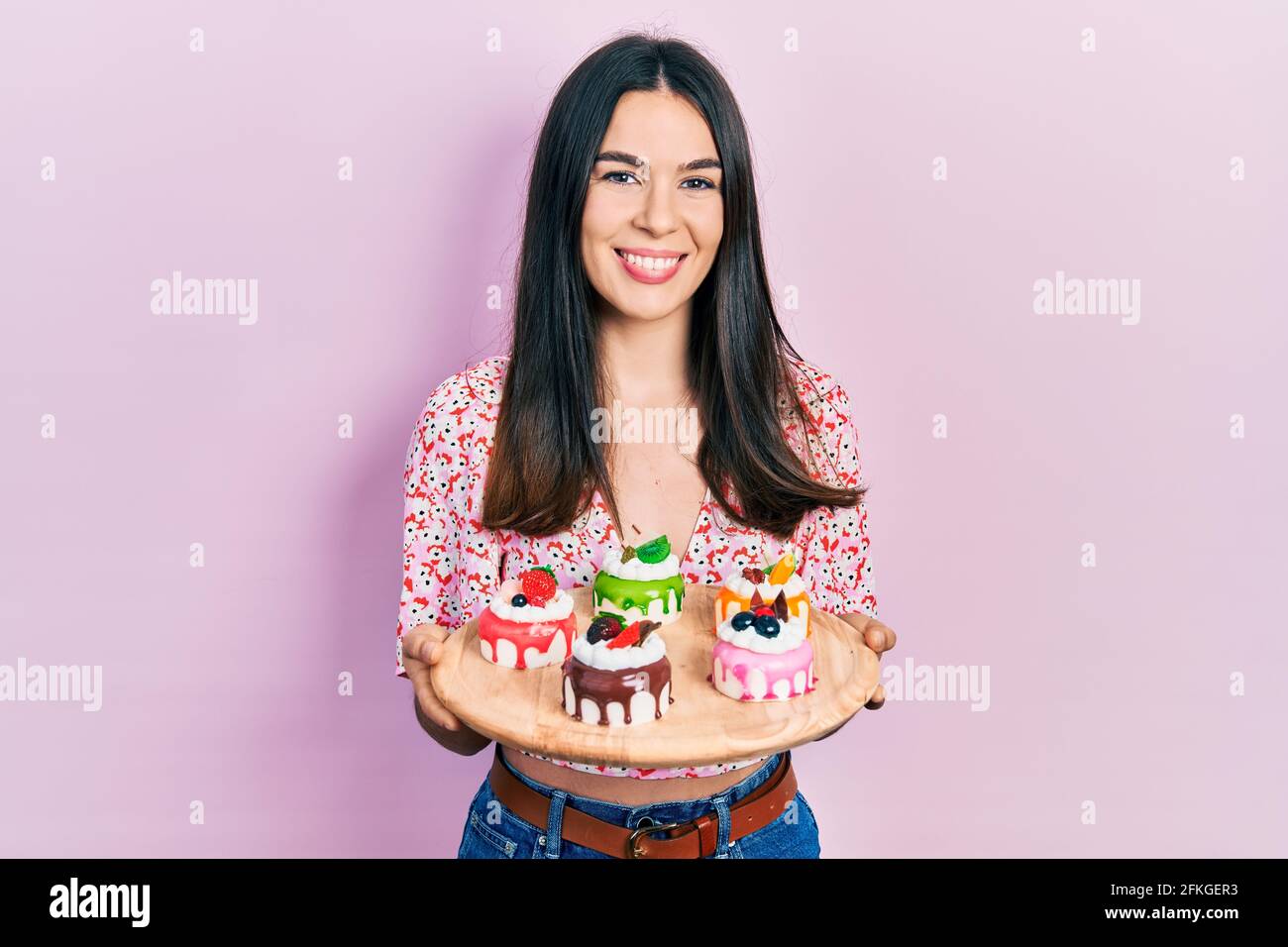 Young brunette woman holding sweet pastries smiling with a happy and ...