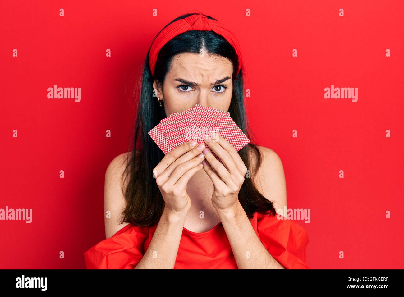 Young brunette woman covering face with cards skeptic and nervous ...