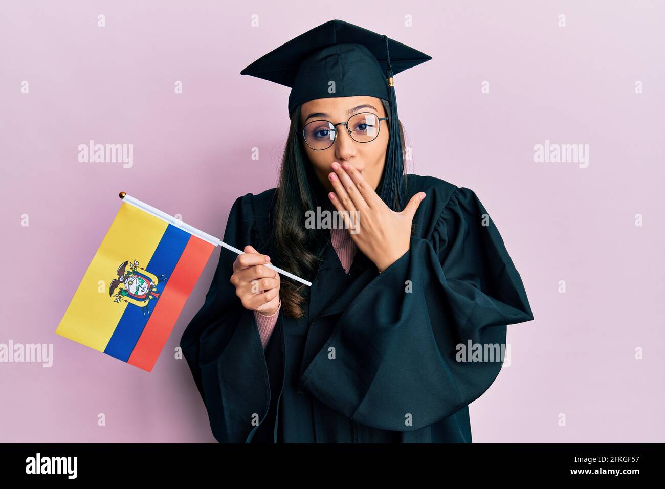 Young hispanic woman wearing graduation uniform holding ecuador flag ...