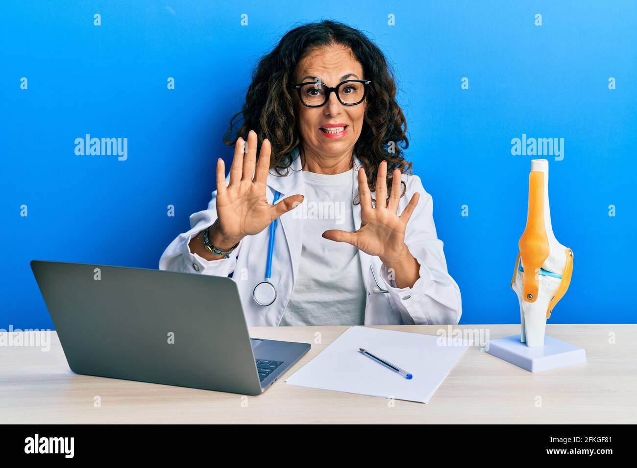 Beautiful middle age woman doctor at orthopedic clinic afraid and ...