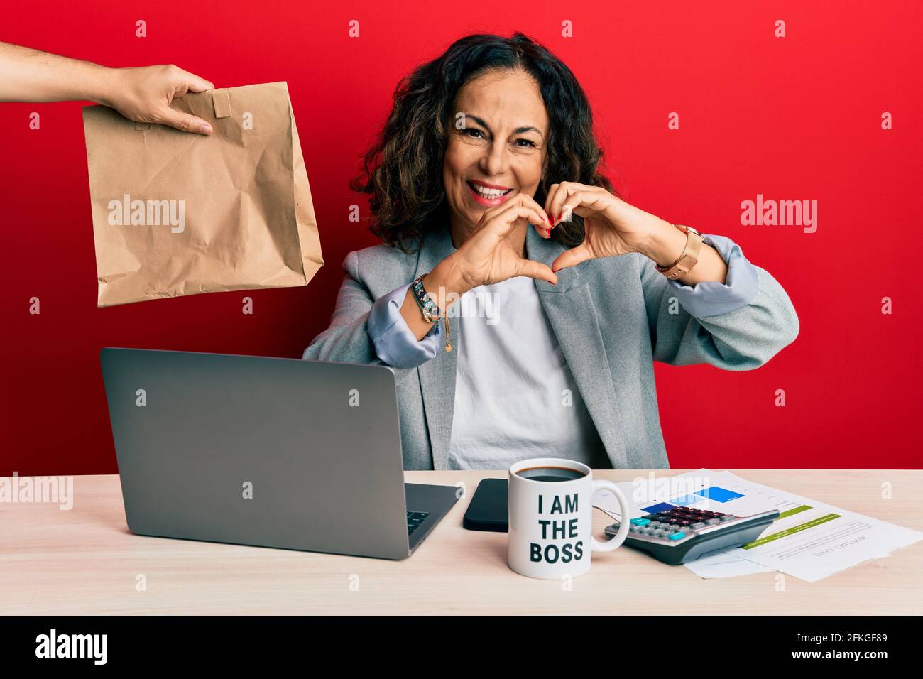 Beautiful middle age woman working at the office ordering delivery food smiling in love doing ...