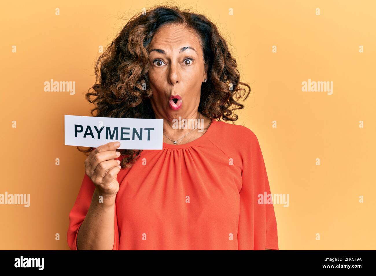 Middle age hispanic woman holding payment word paper scared and amazed ...
