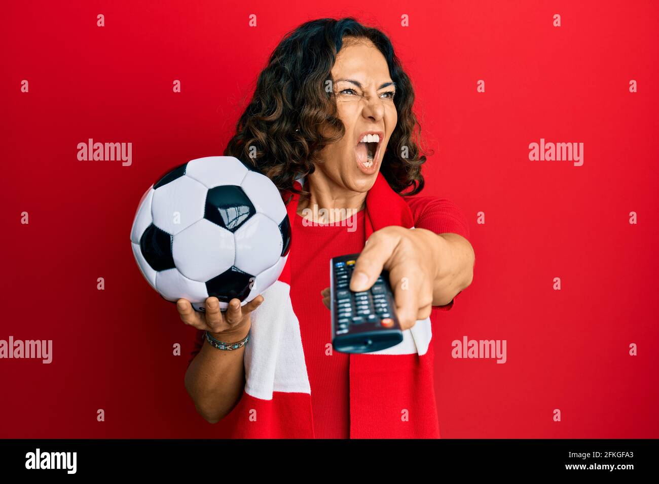 Middle age hispanic woman football hooligan holding ball using tv ...