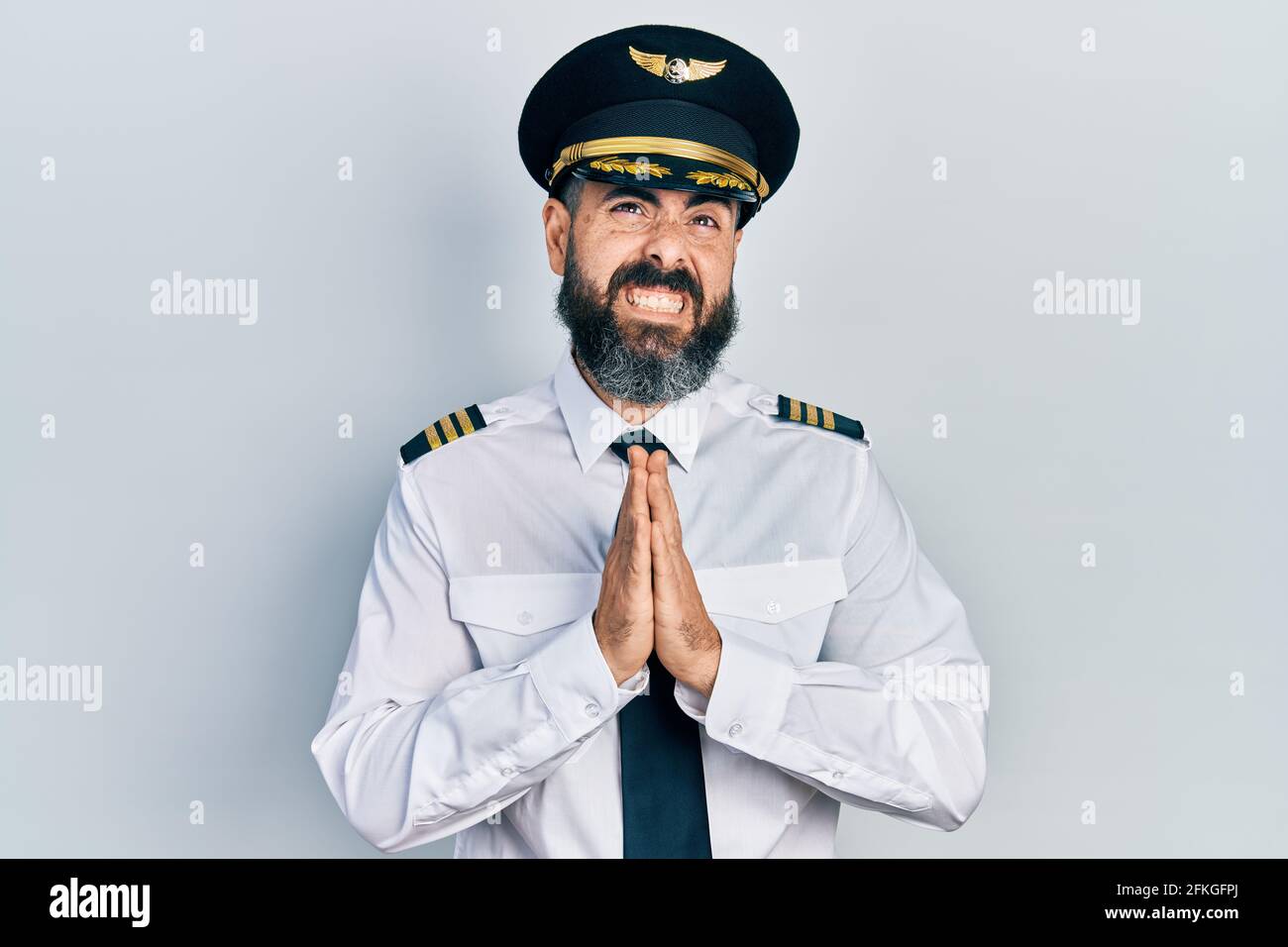Young hispanic man wearing airplane pilot uniform begging and praying ...