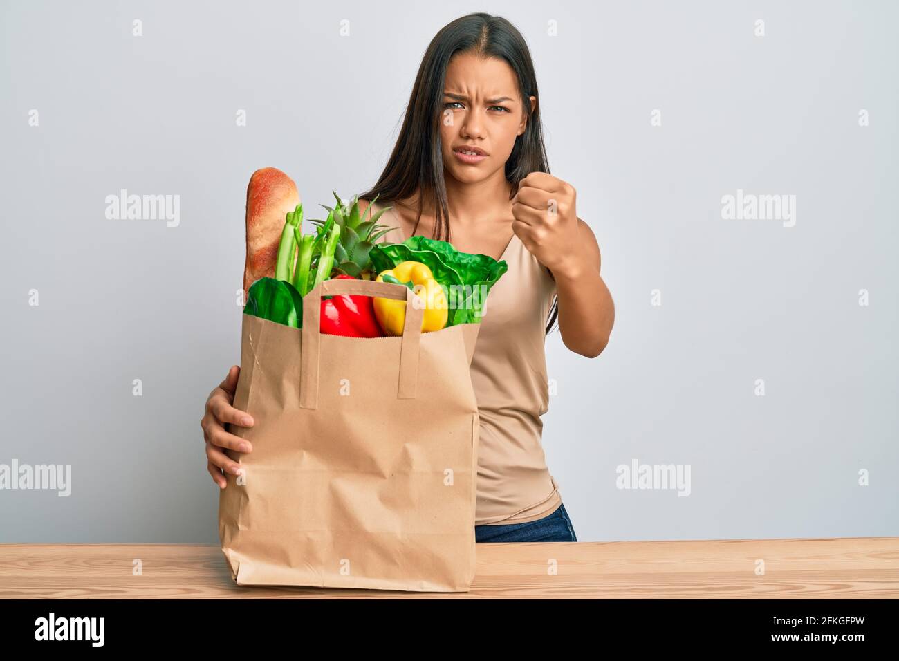 Beautiful hispanic woman holding paper bag with bread and groceries ...