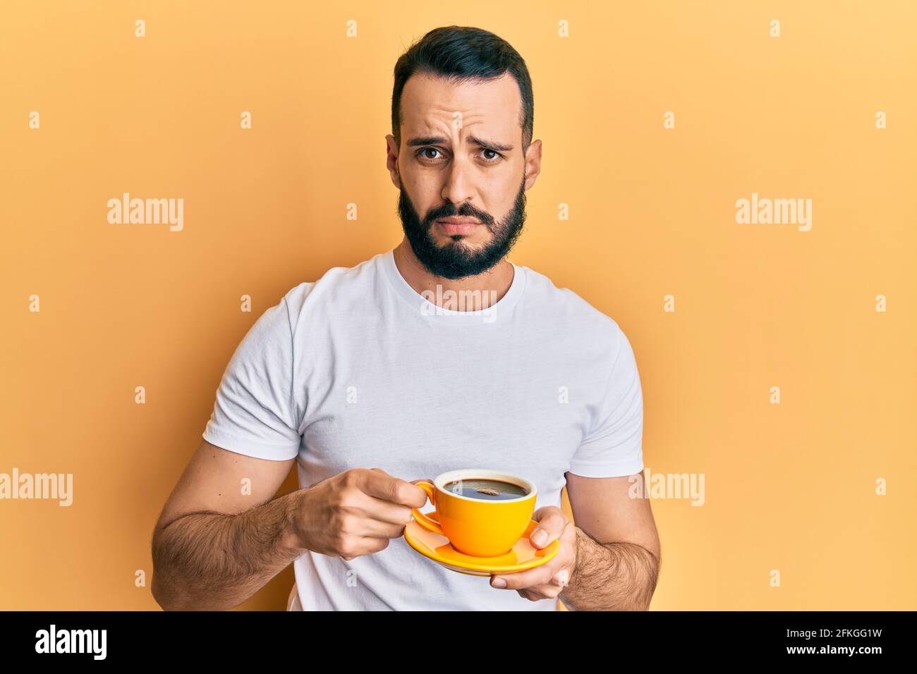 Young man with beard drinking a cup coffee skeptic and nervous ...