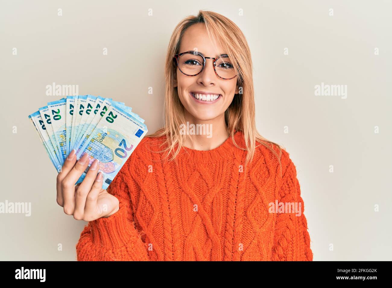 Beautiful blonde woman holding 20 euro banknotes looking positive and ...