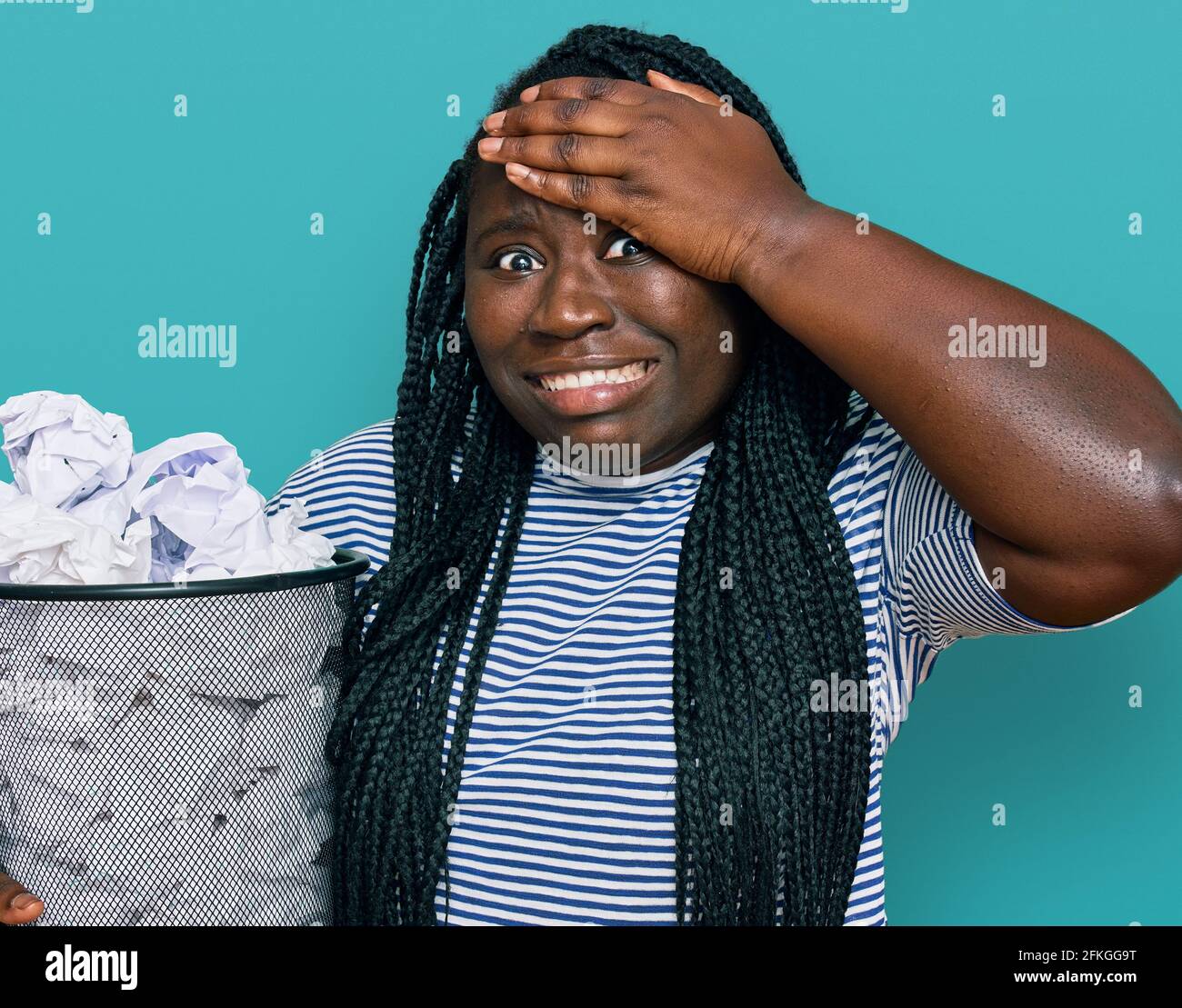 Young black woman with braids holding paper bin full of crumpled papers ...