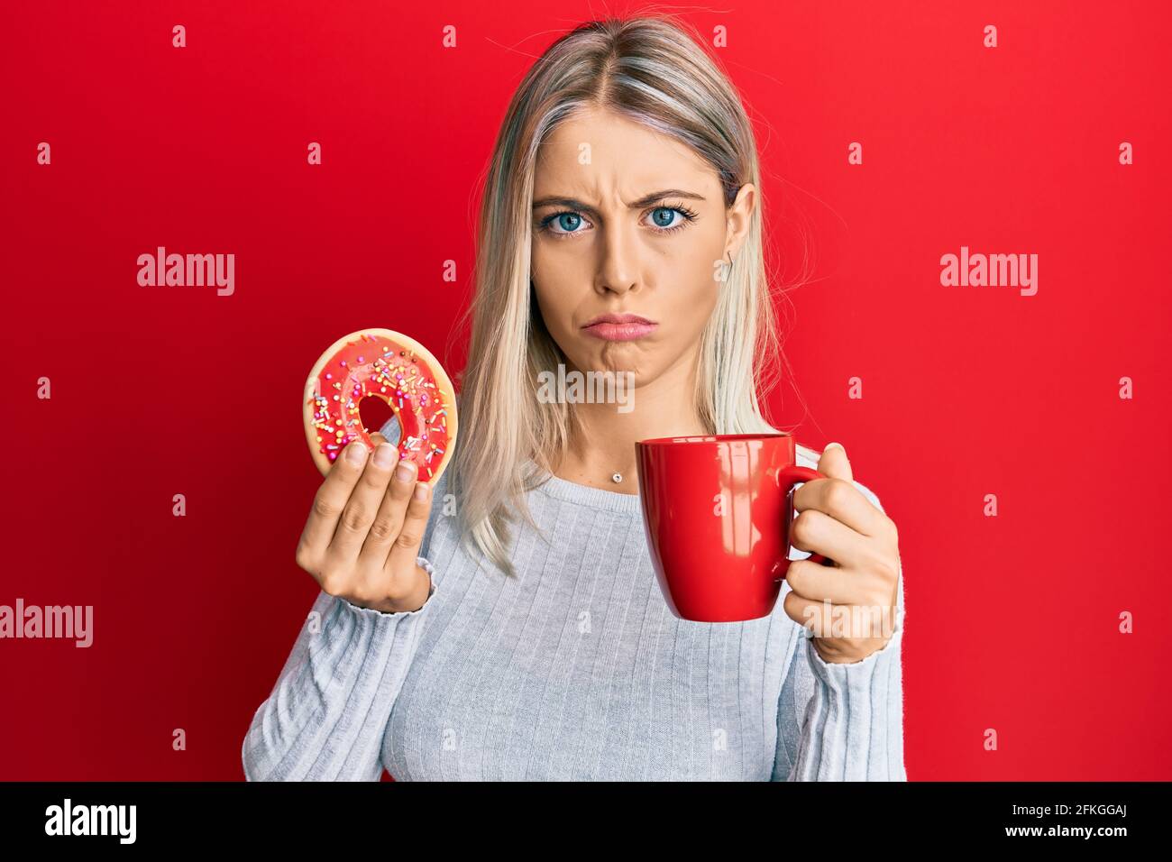 Beautiful blonde woman eating doughnut and drinking coffee depressed ...