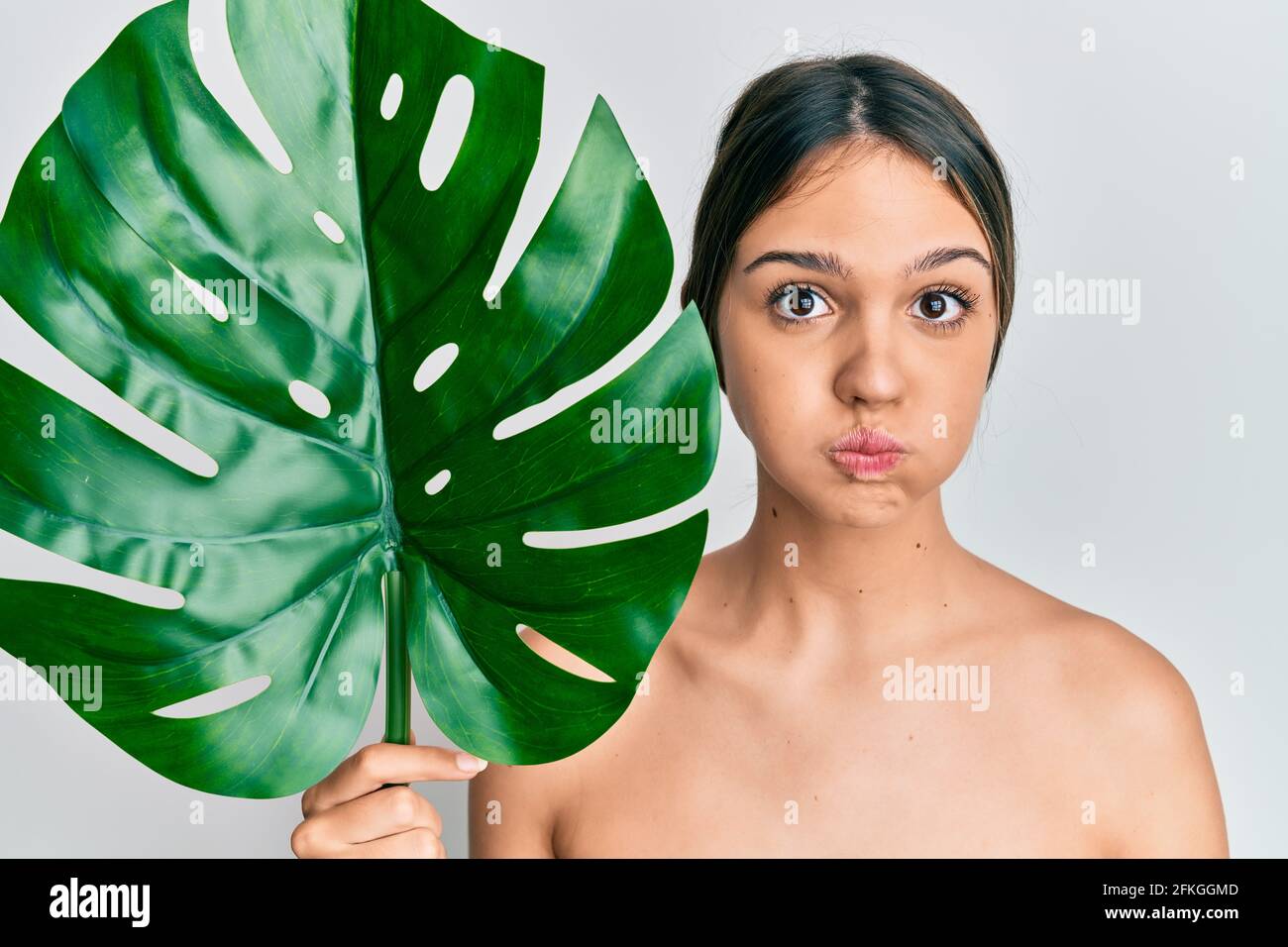 Young brunette woman holding green plant leaf close to beautiful face ...