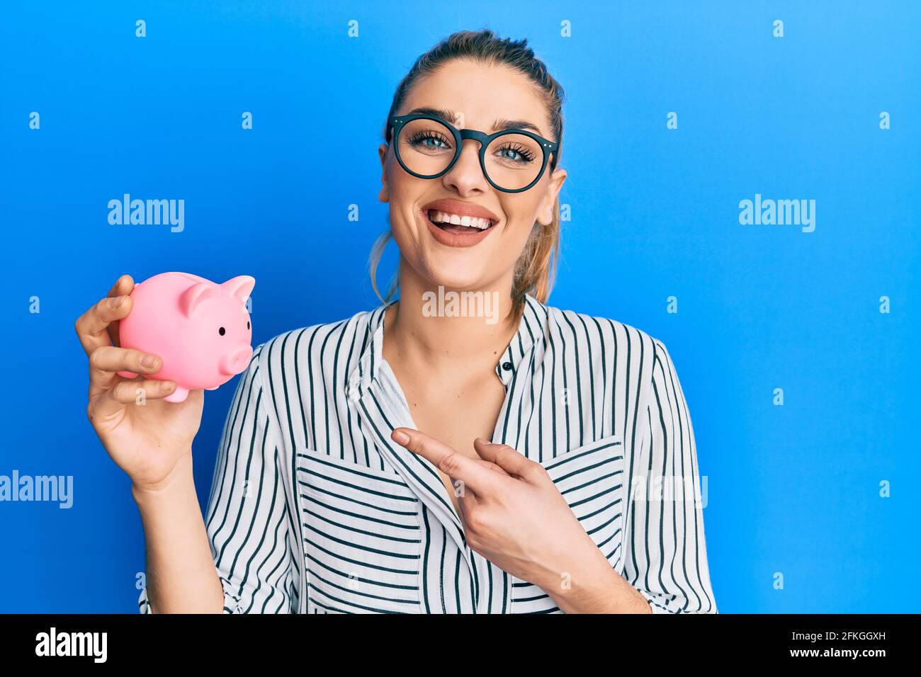 Young caucasian woman wearing business clothes holding piggy bank ...