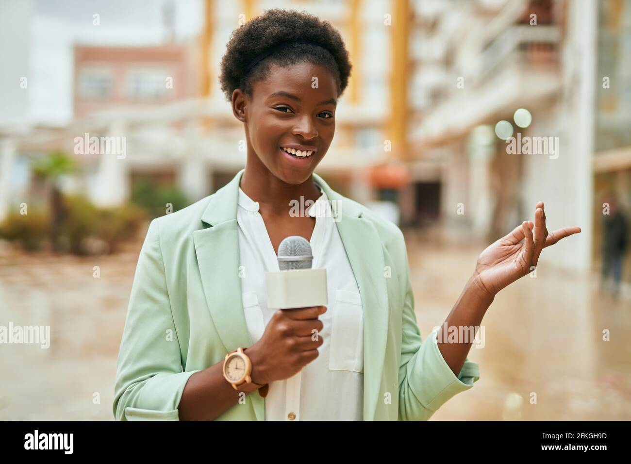 Young african american reporter woman using microphone at the city ...