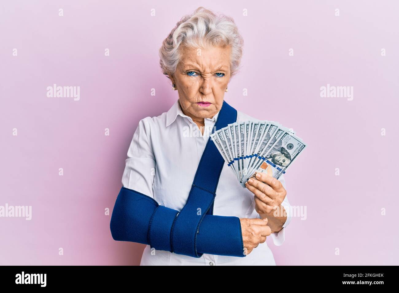 Senior grey-haired woman wearing arm on sling holding usa dollars ...