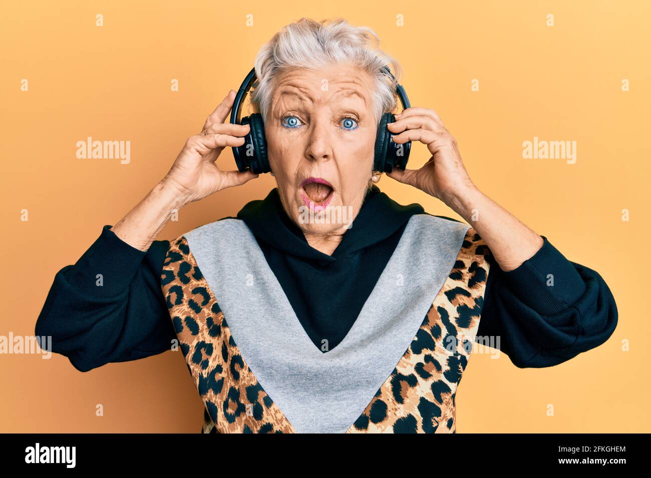 Senior grey-haired woman listening to music using headphones afraid and ...