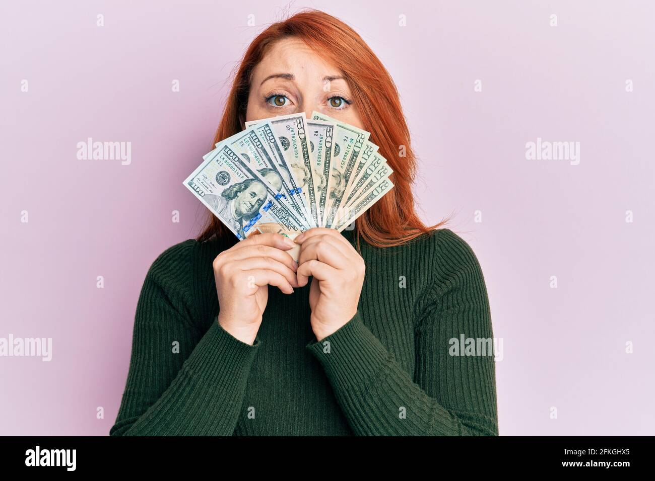Beautiful redhead woman holding dollars close to face depressed and ...