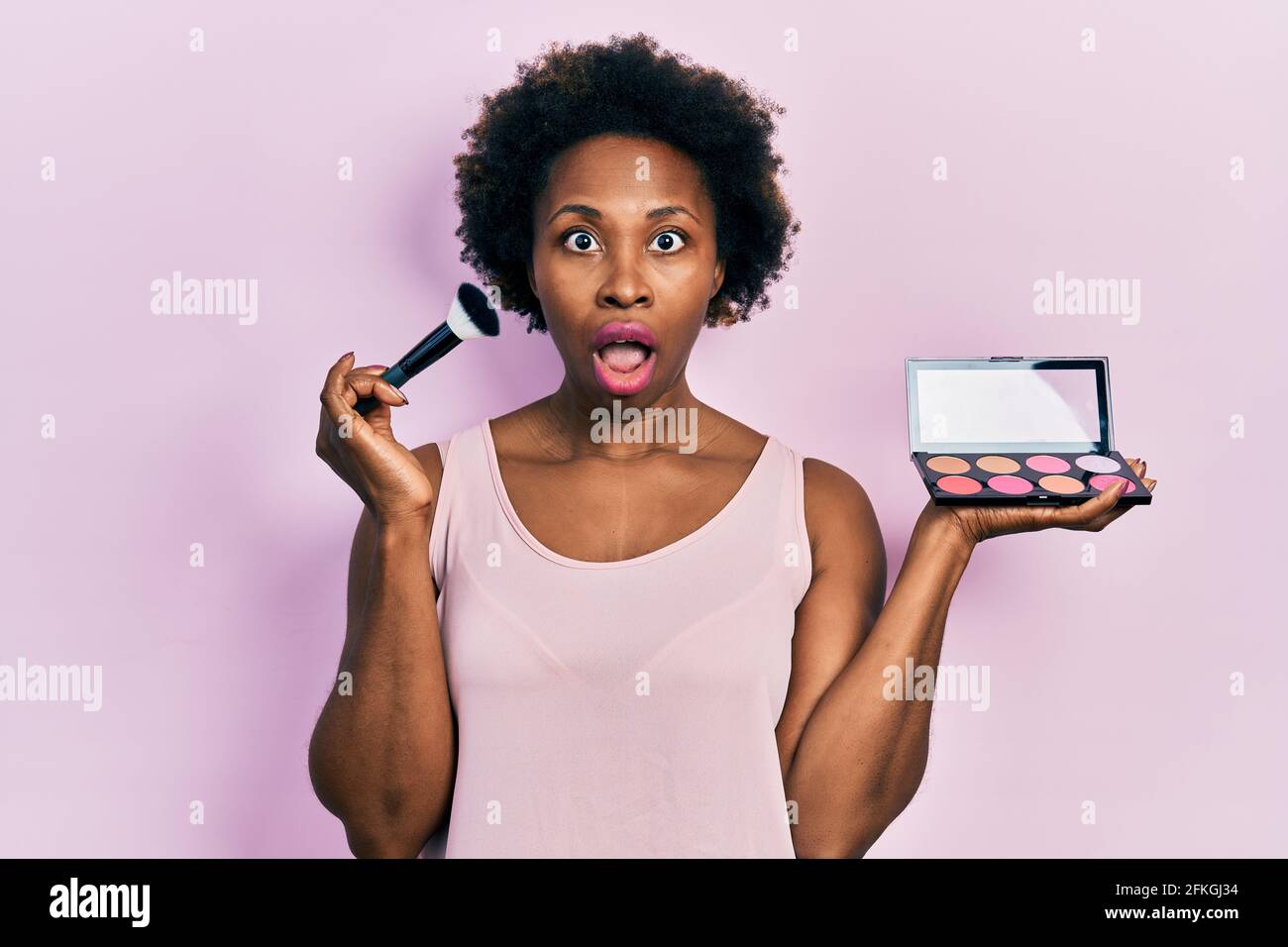 Young african american woman holding makeup brush and blush afraid and ...
