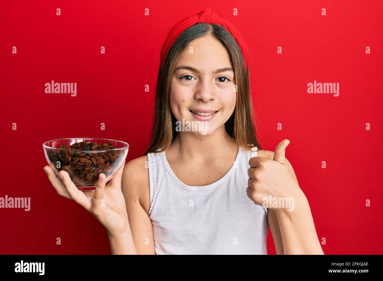 Beautiful brunette little girl holding bowl of raisins smiling happy ...